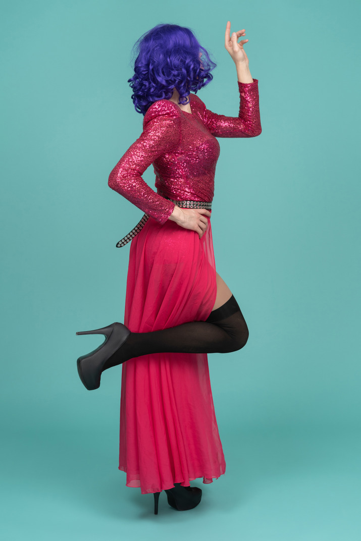 Side view of a drag queen in pink dress raising a leg & pointing ...