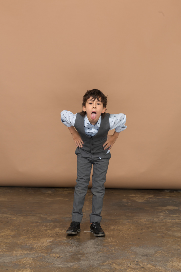 Front view of a boy in suit standing with hands on hips and bending ...