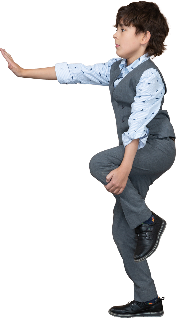 Side view of a boy in suit standing on one leg with extended arm Photo