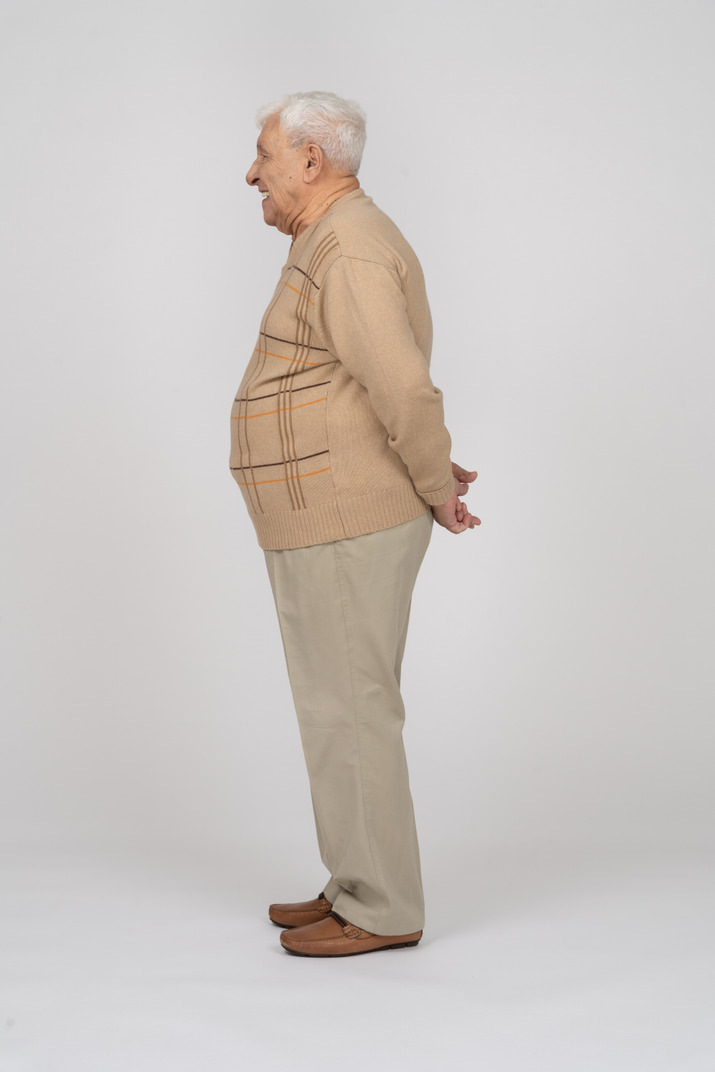 Side view of an old man in casual clothes standing with hands behind ...