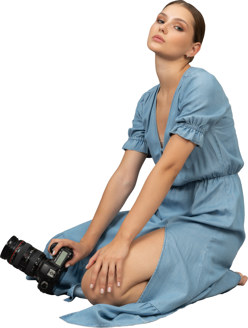 Side view of a young woman in blue dress sitting on a floor with camera ...